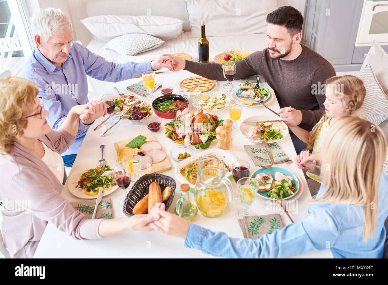 High angle portrait of big happy family joining hands in prayer at ...
