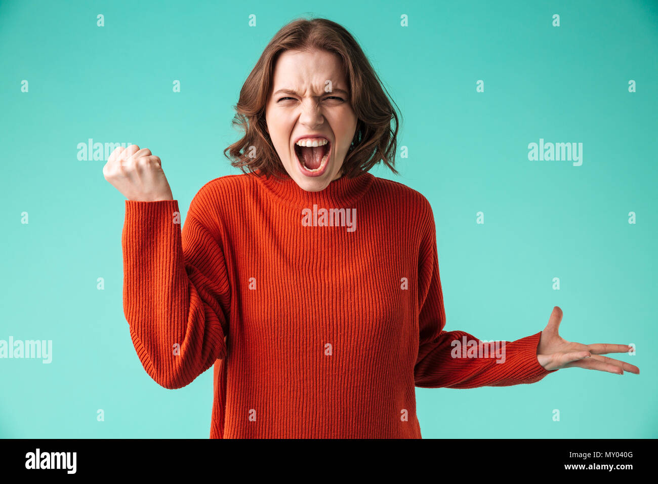 Portrait of an angry young woman dressed in sweater screaming isolated ...