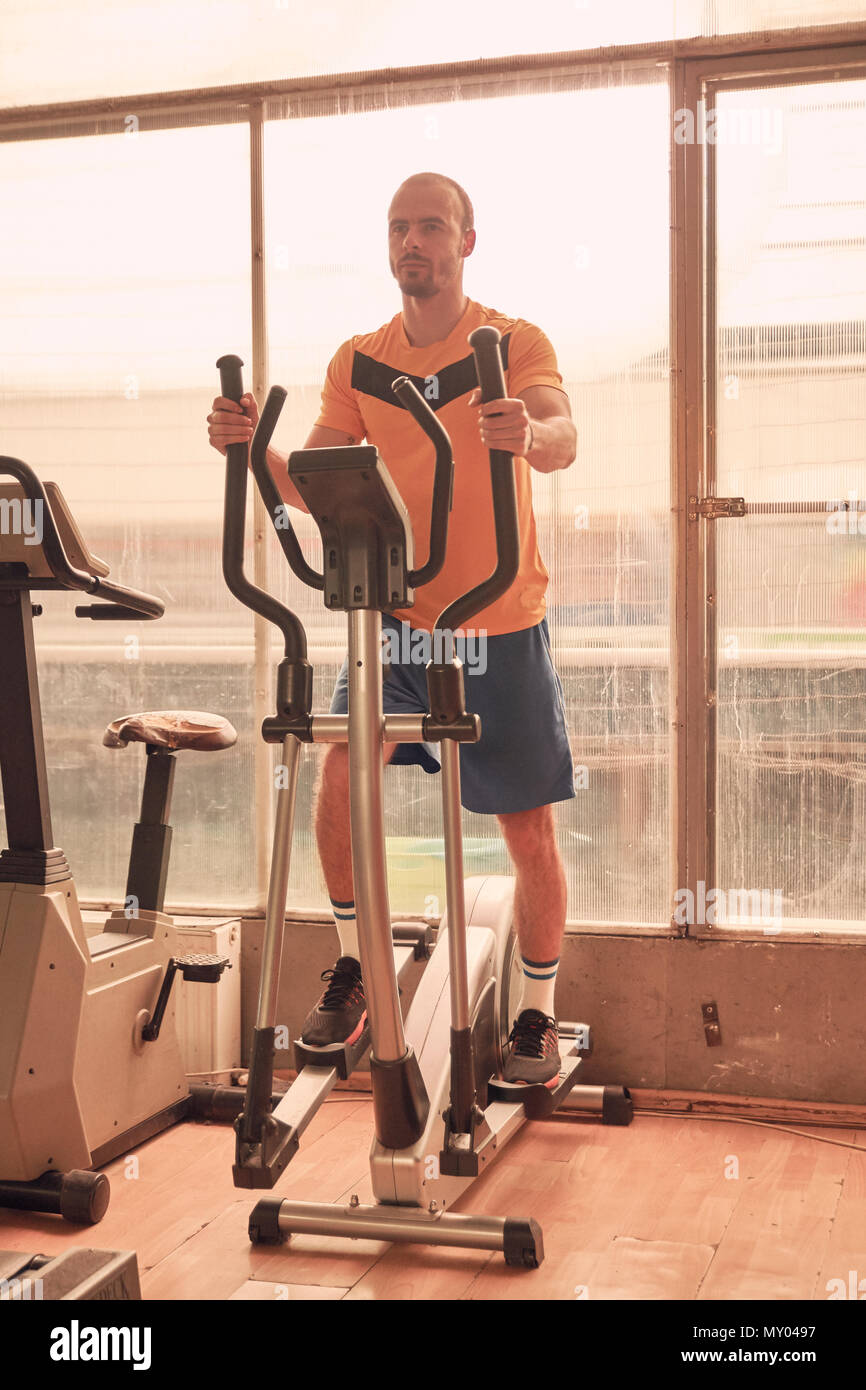 one young man, wearing sport clothes, traning on elliptical, old beaten ...