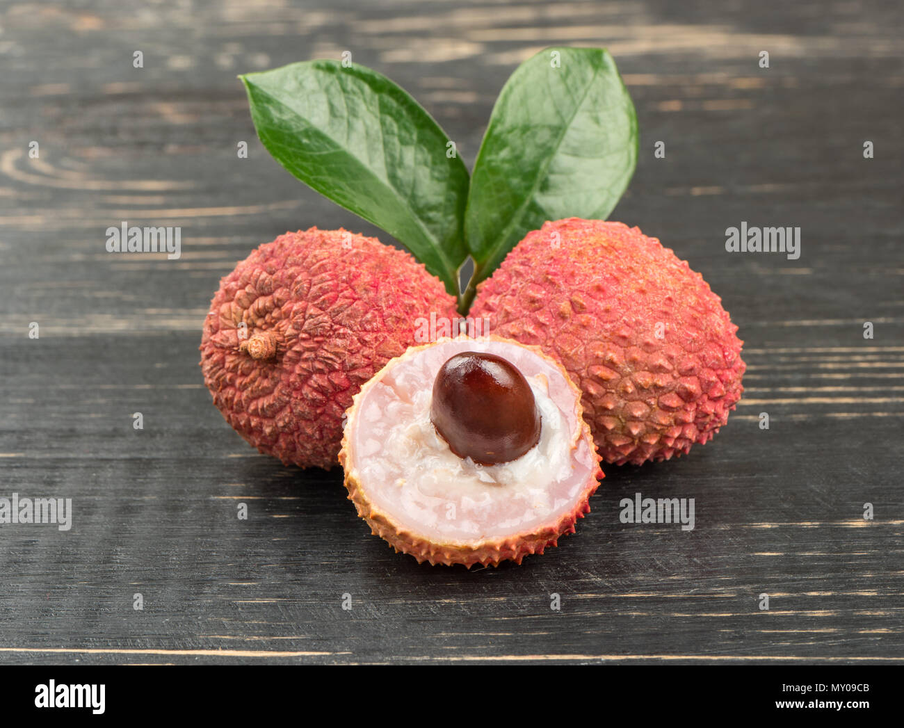 Two lychee fruit in the shell with half and leaves on wooden background ...