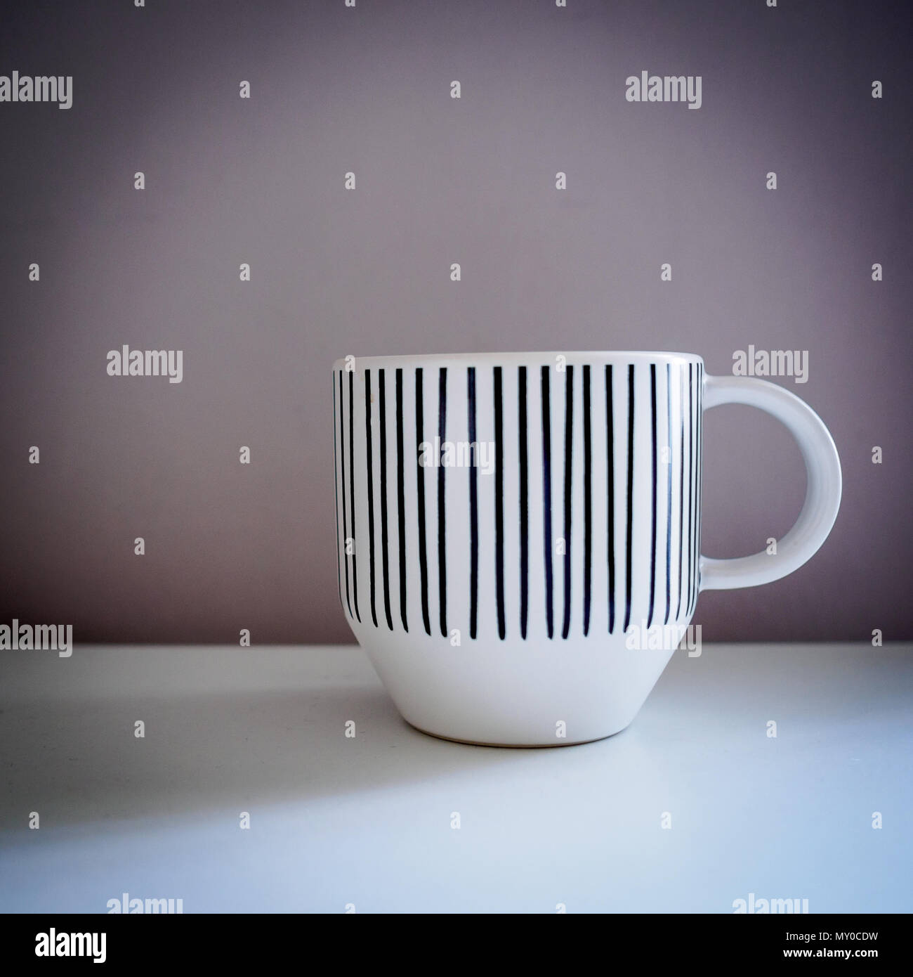White mug with black lines decorations on a white table. Vintage look ...