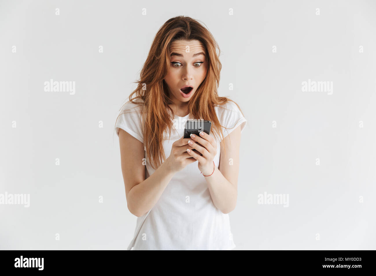 Portrait of a shocked young girl holding mobile phone isolated over ...
