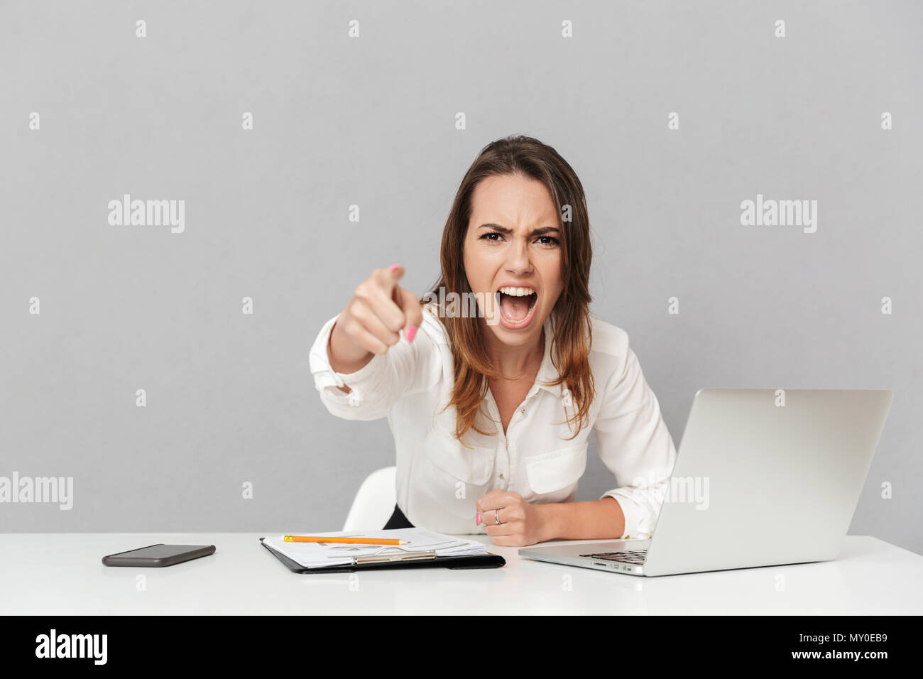 Portrait of a mad young business woman sitting at the office desk and ...