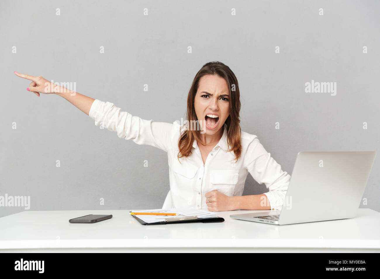 Portrait of an angry young business woman sitting at the office desk ...