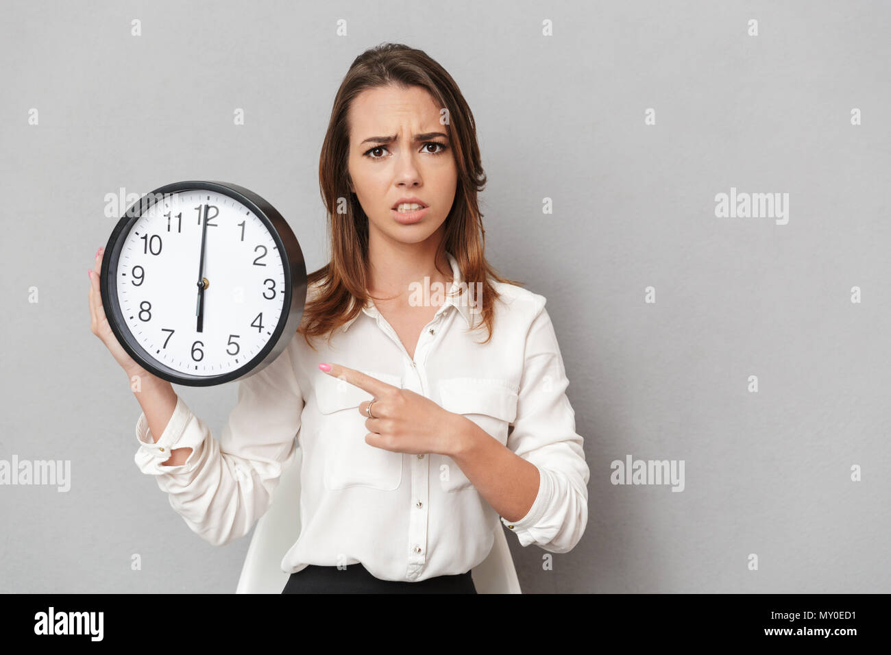 Portrait of a confused young business woman pointing finger at alarm ...
