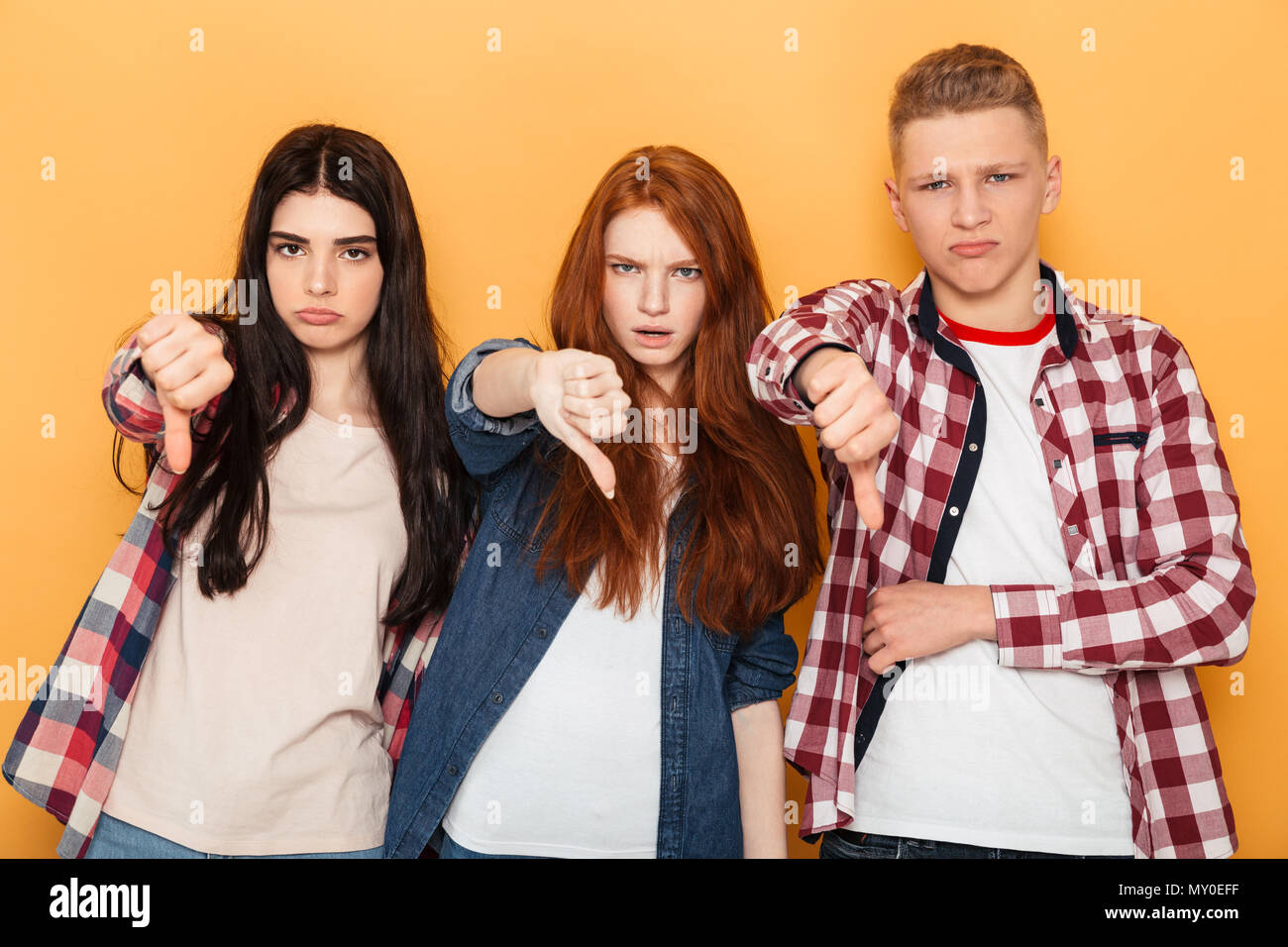 Group of disappointed school friends showing thumbs down while standing ...
