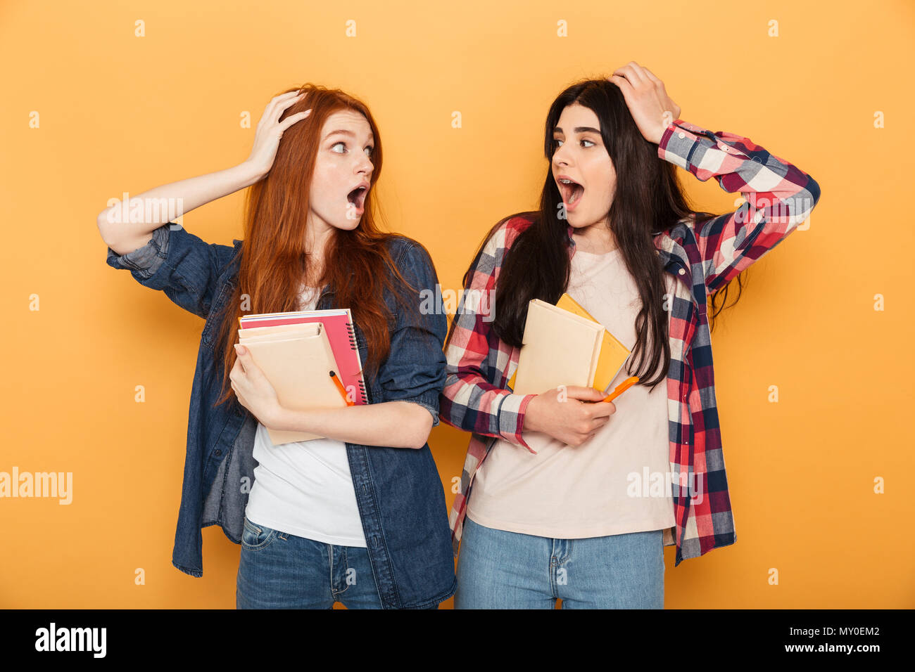 Portrait of two surprised young school teenage girls holding copybooks ...
