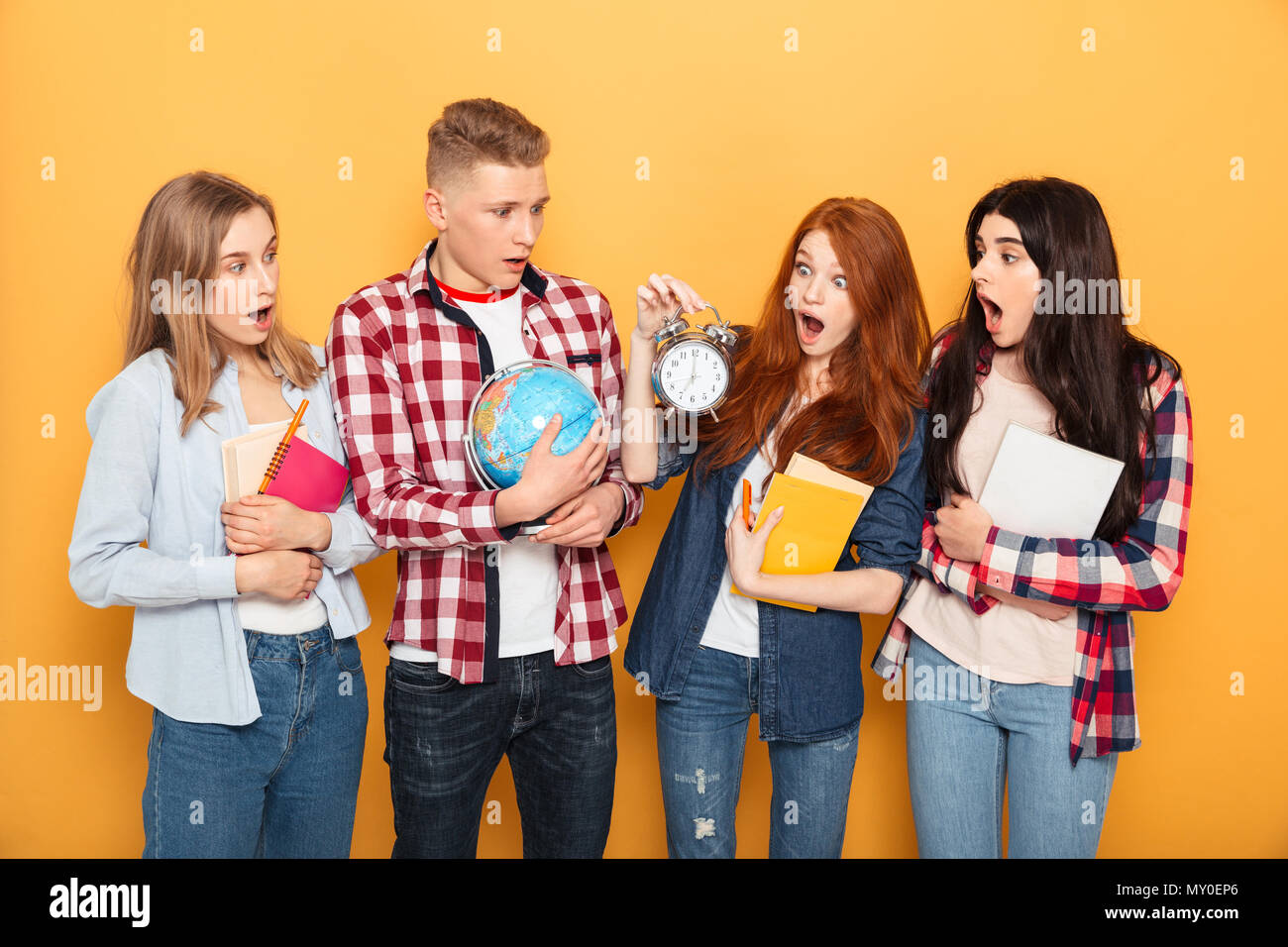 Group of shocked school friends holding alarm clock and screaming over ...