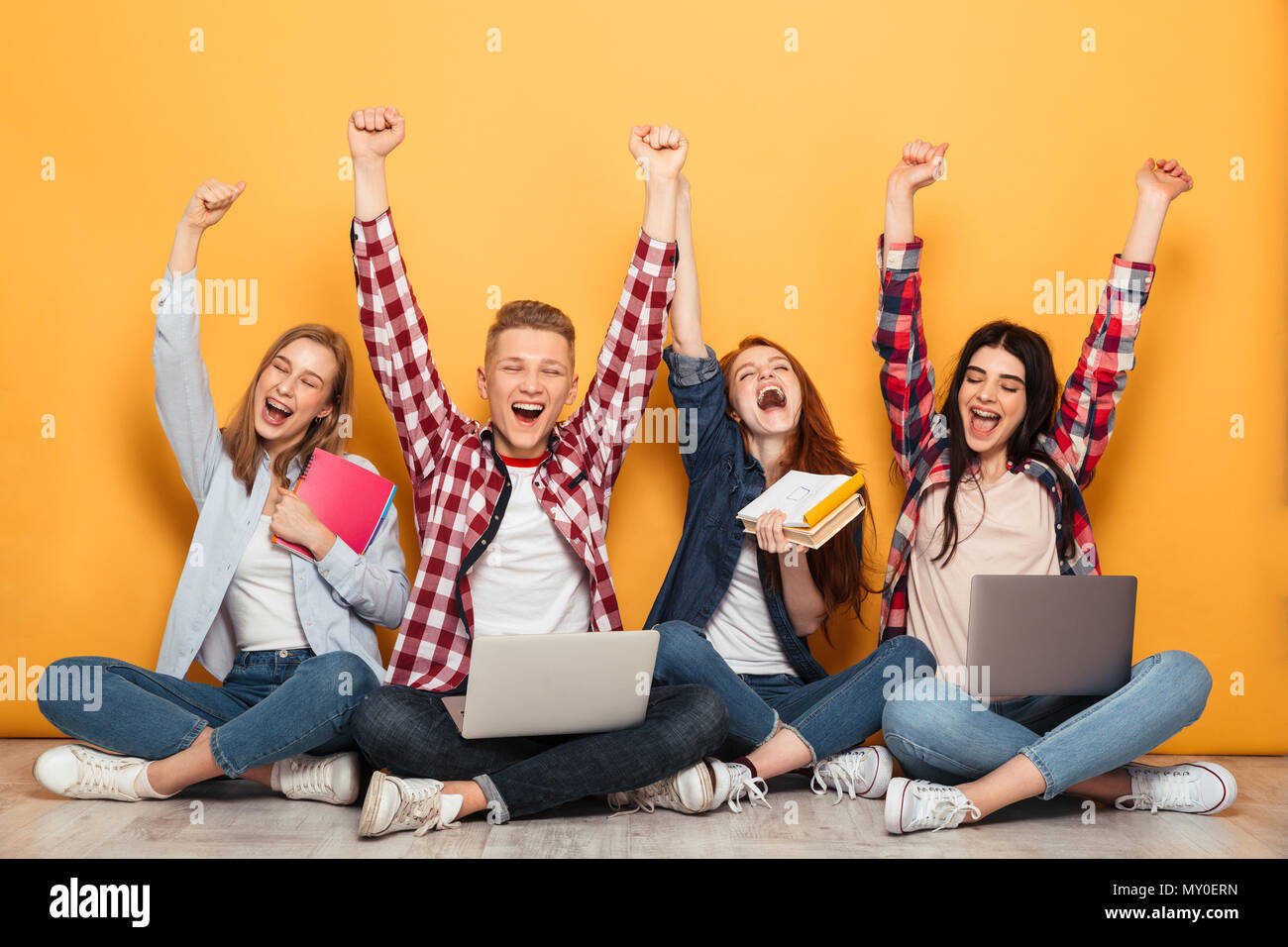 Group of young cheerful school friends doing homework while sitting on ...