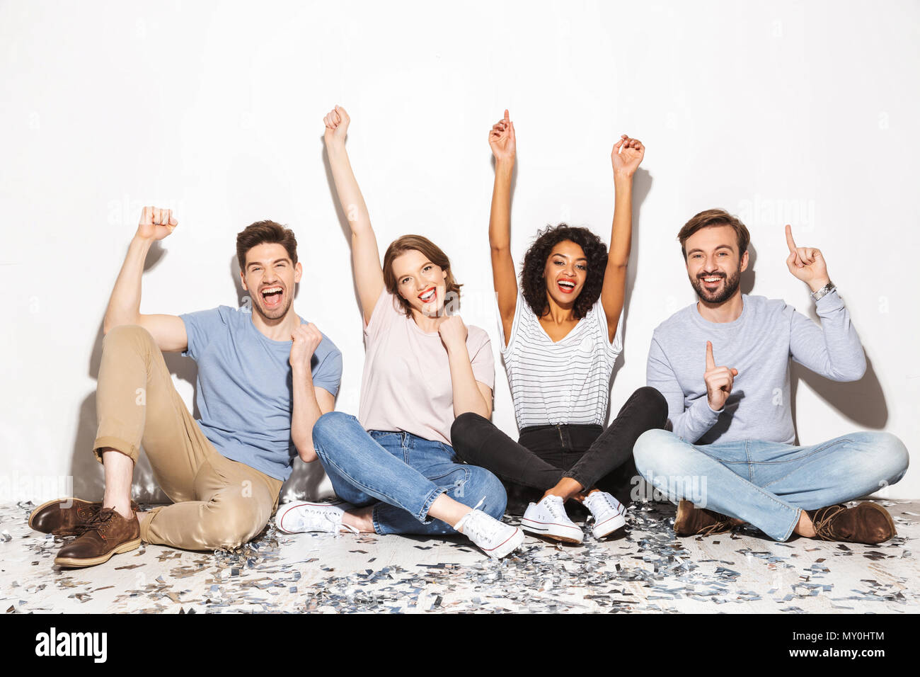 Group of happy multiracial people sitting on a floor with confetti and ...