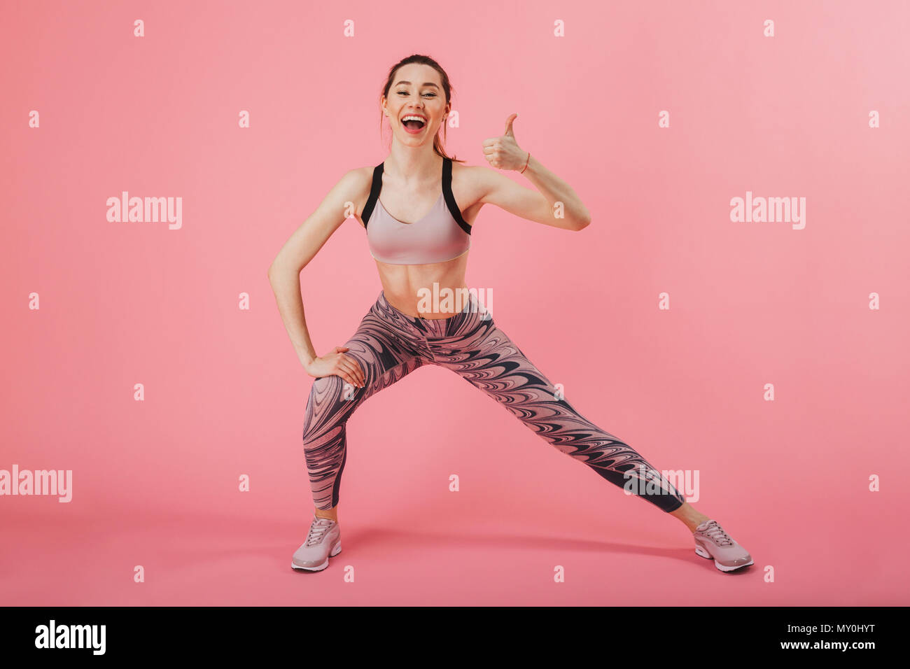 Full length image of Happy sportswoman doing exercise and showing thumb ...