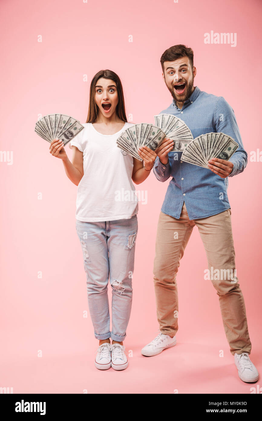 Full length portrait of an excited young couple holding bunch of money ...