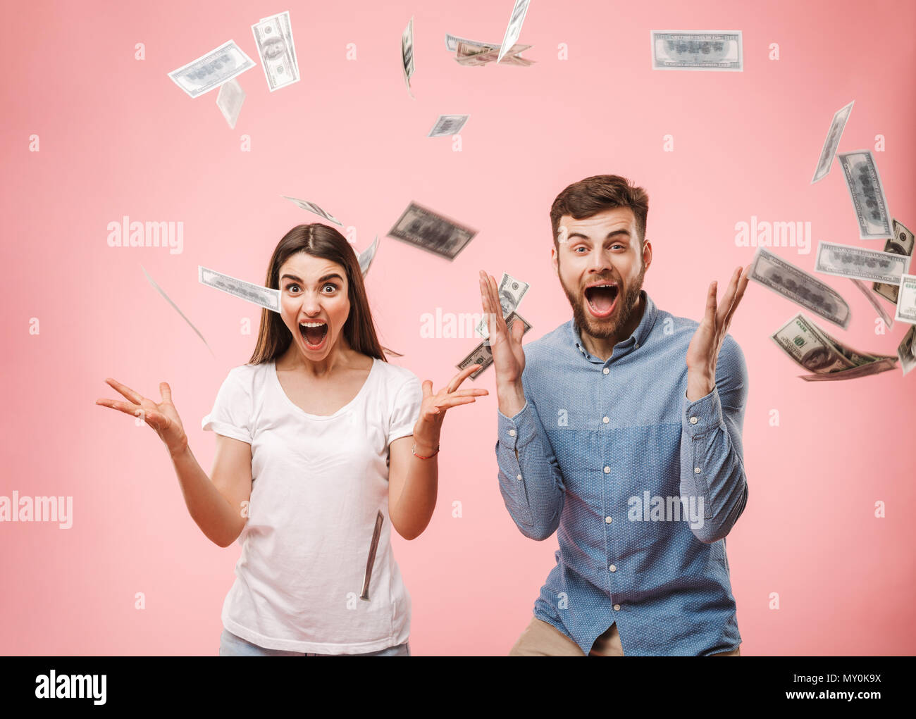 Portrait of a joyful young couple standing under money banknotes shower ...
