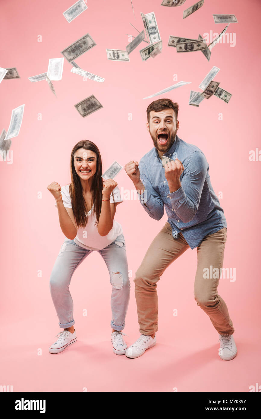 Full length portrait of an excited young couple standing under money ...