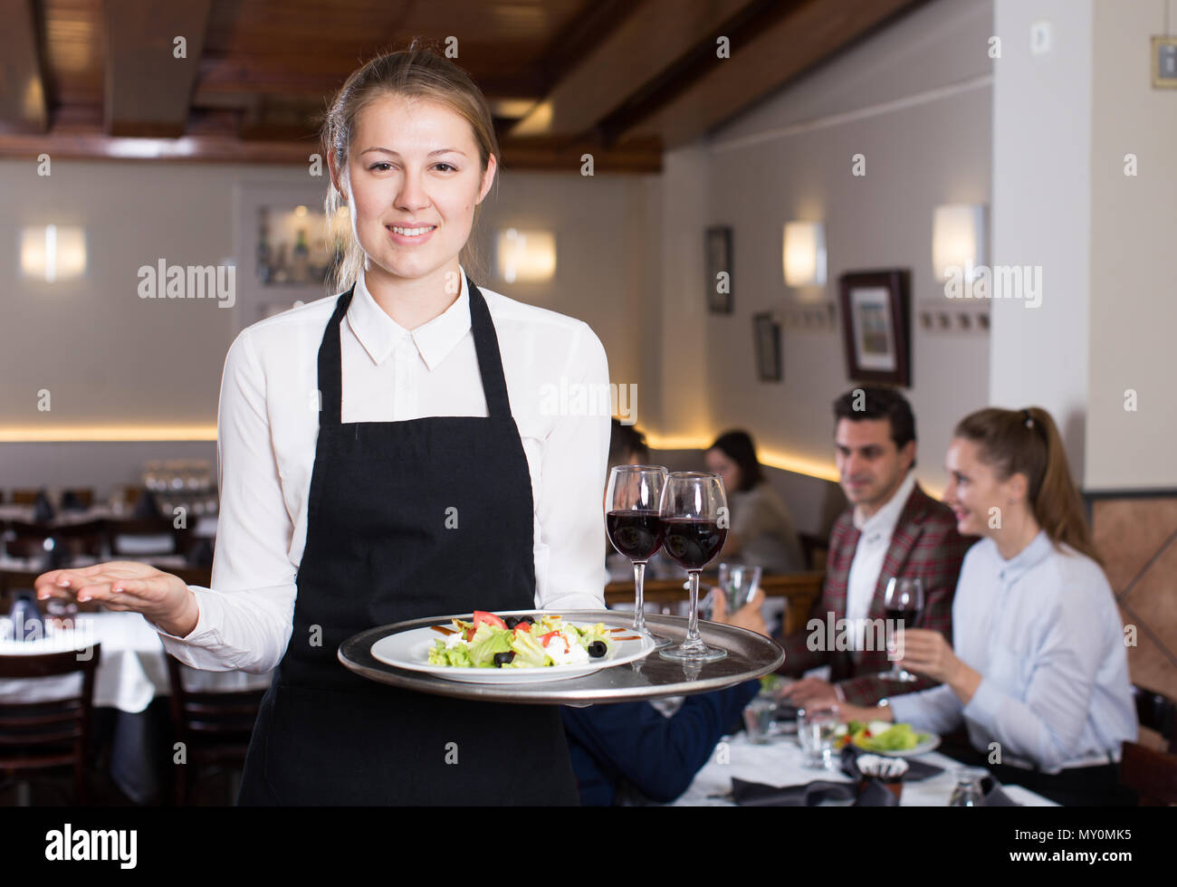 Portrait of smiling waitress with serving tray meeting restaurant ...