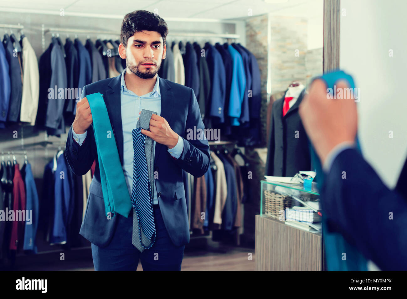 Man is picking up tie for jacket in front of the mirror in men's shop ...