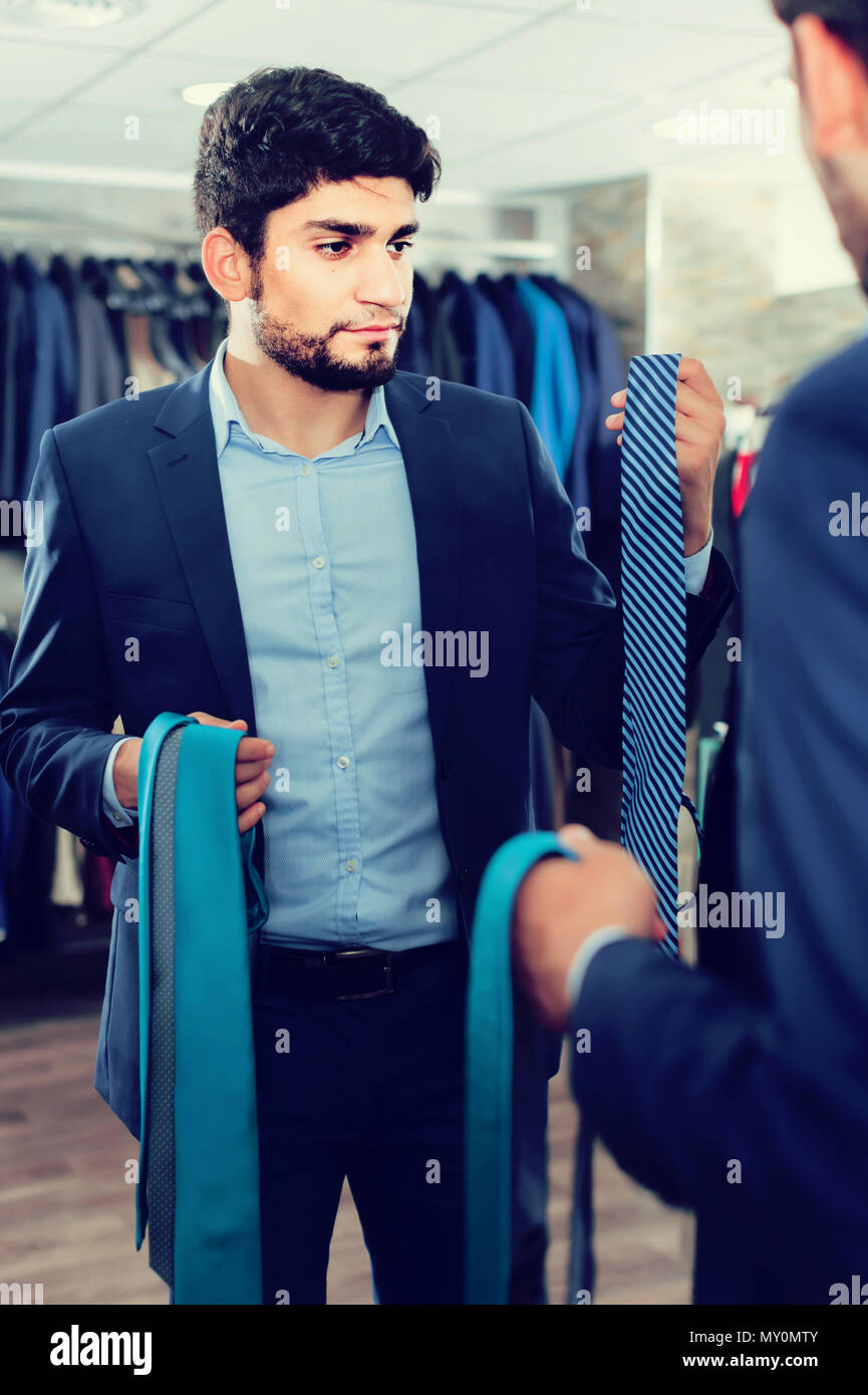 Customer man is picking up tie for jacket in front of the mirror in men ...