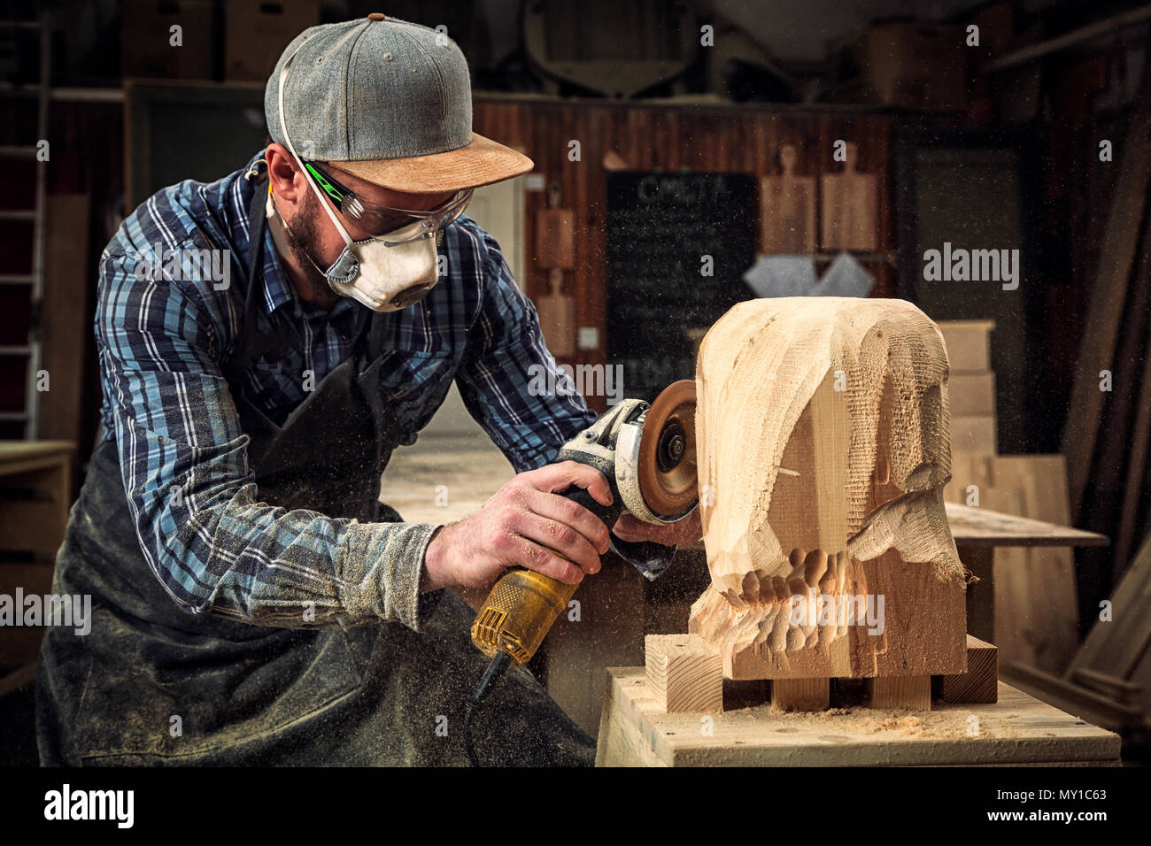 A young man carpenter in a suit, goggles saws a man's head with a tree ...