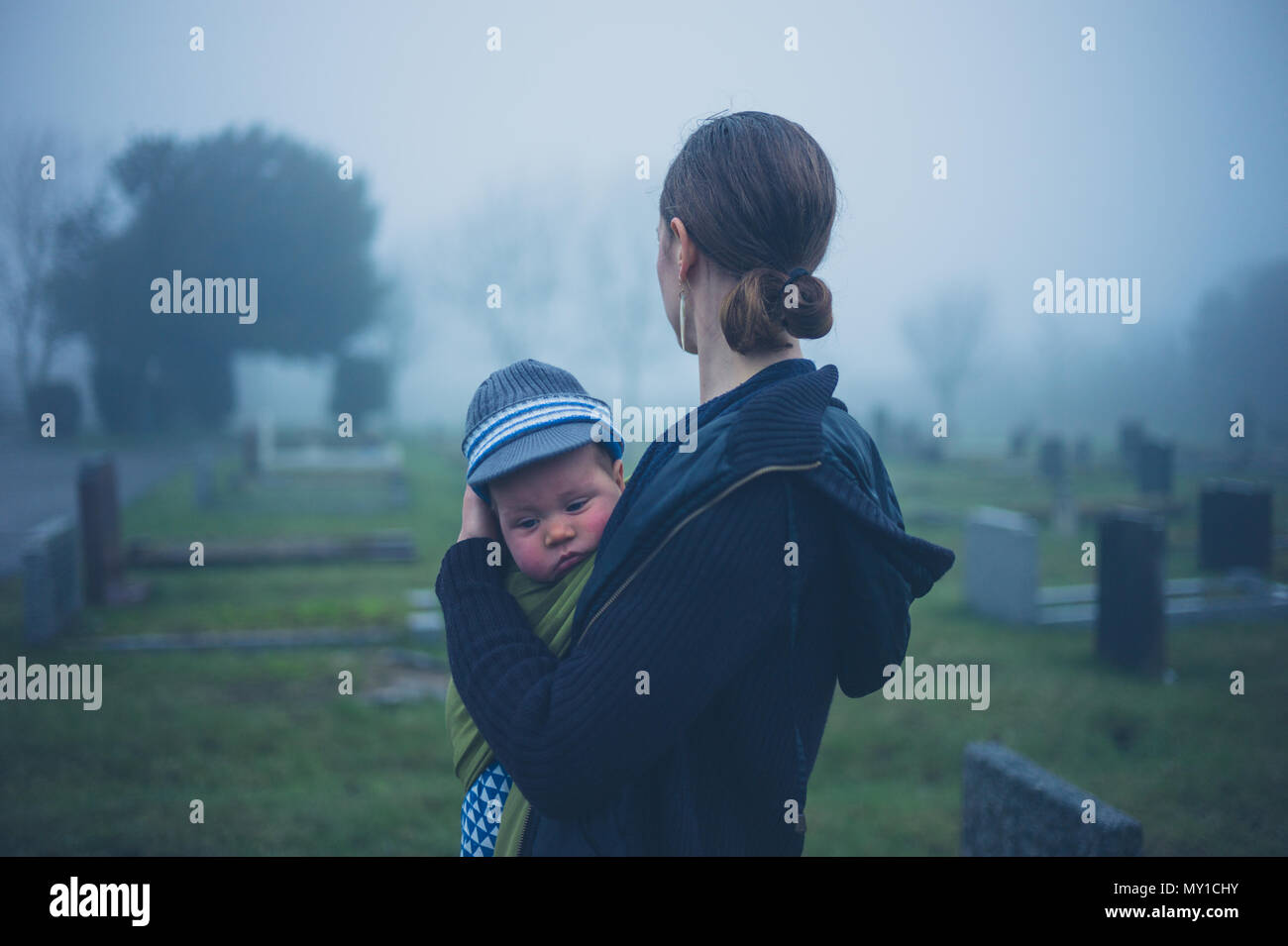 A grieving young mother is standing with her baby by a tombstone in a ...