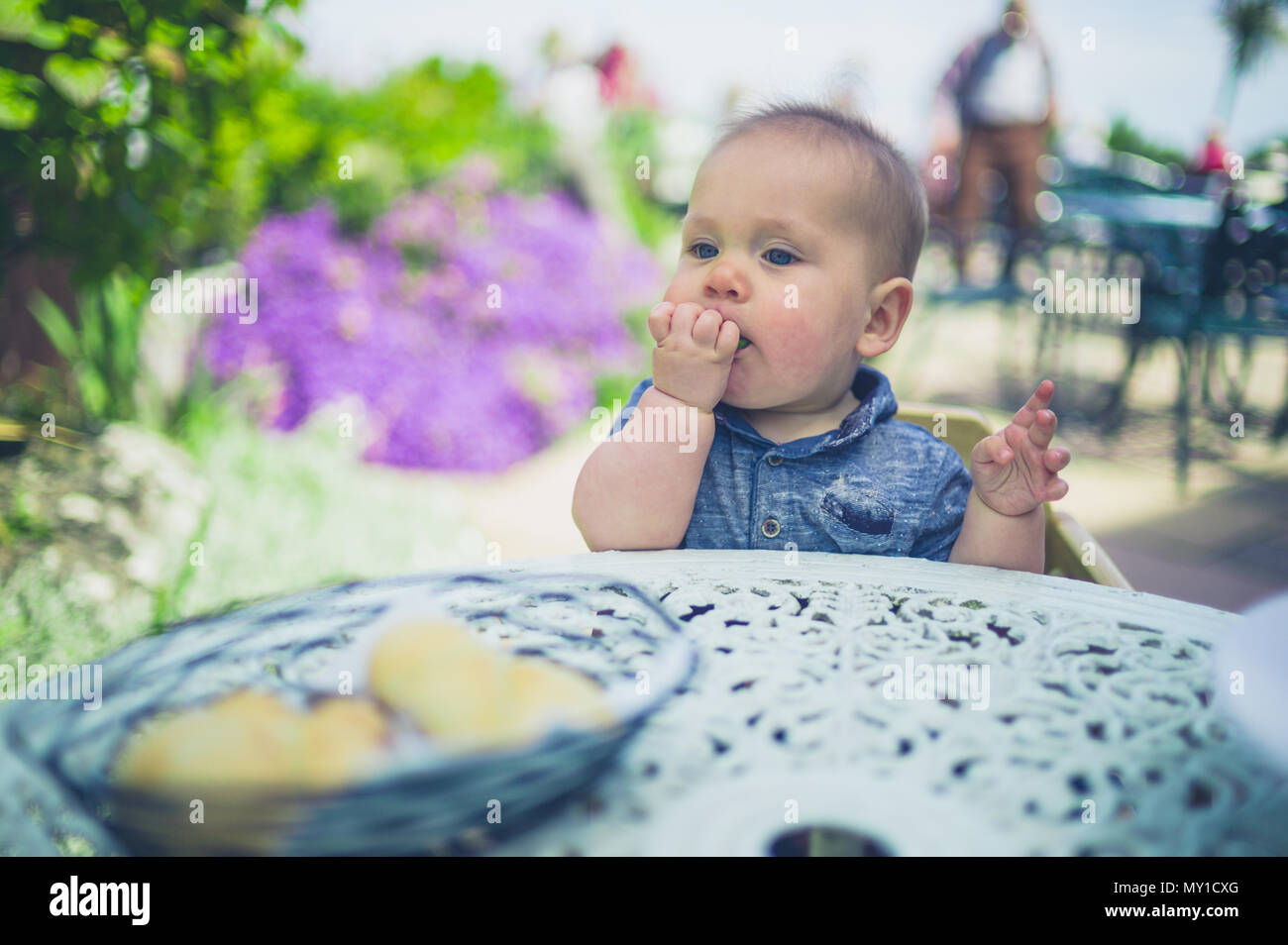 A little baby is sitting a t a table outside eating Stock Photo - Alamy