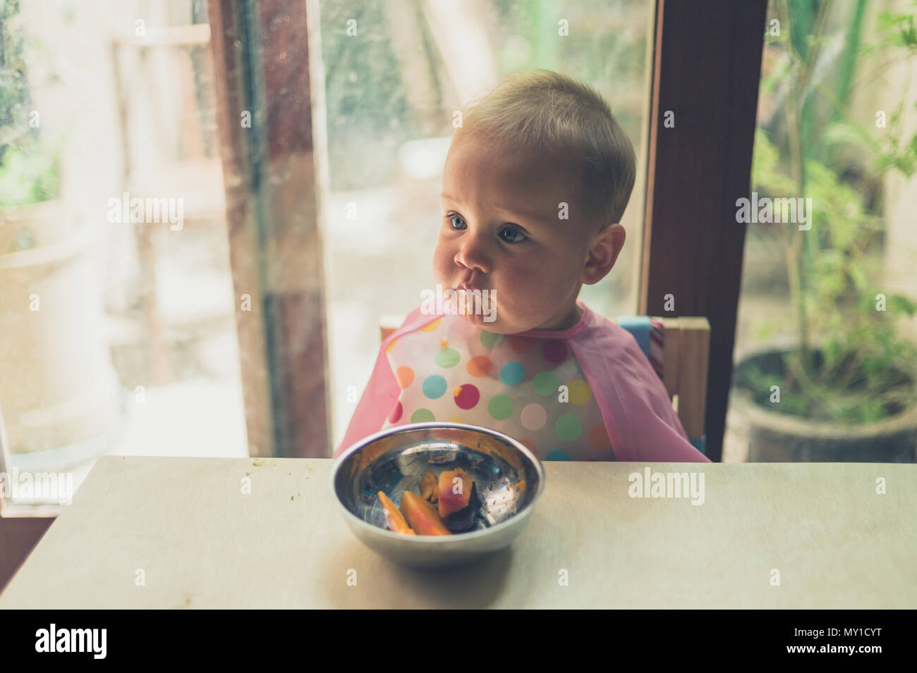 A little baby wearing an apron is learning how to eat at the table ...