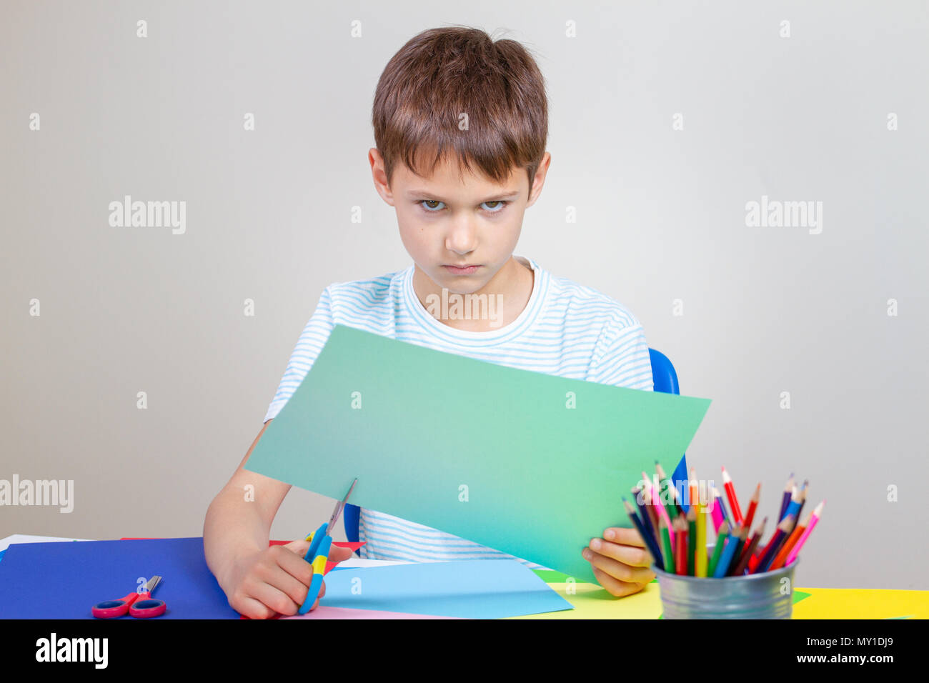 Angry child cutting colored paper with scissors at the table Stock ...