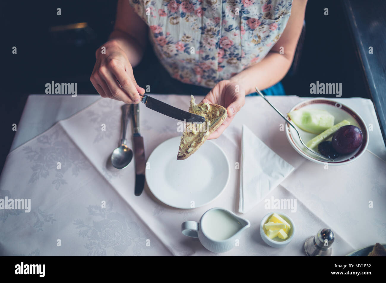 A young woman is eating toast with butter at a dining table Stock Photo ...