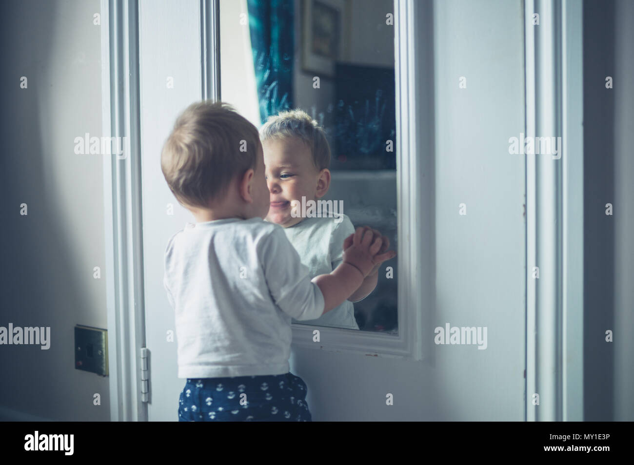 A cute little baby is playing with his own reflection Stock Photo - Alamy