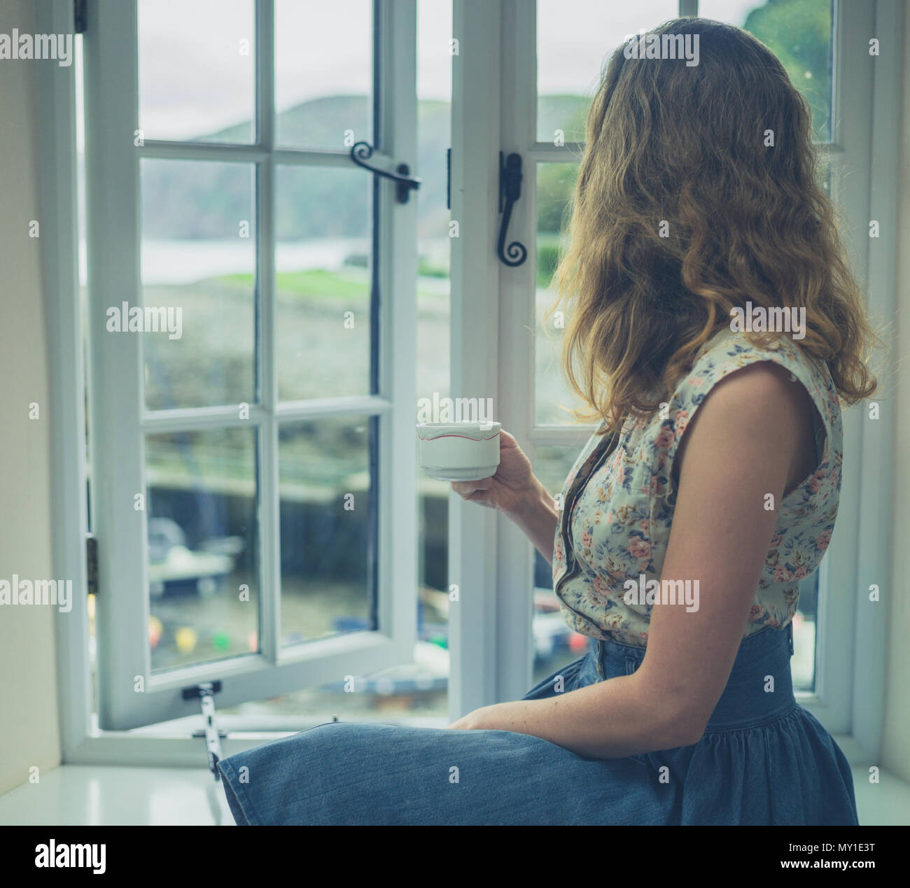 A young woman is drinkng tea by the window of a country house Stock ...