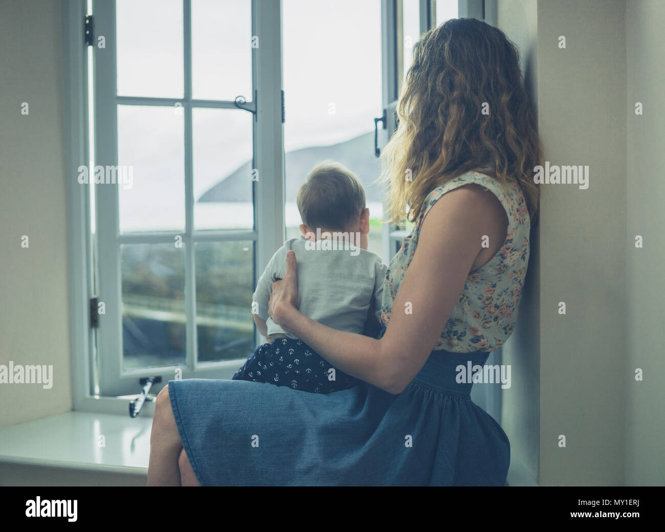 A young mother and baby are sitting by the window of a rural home Stock ...