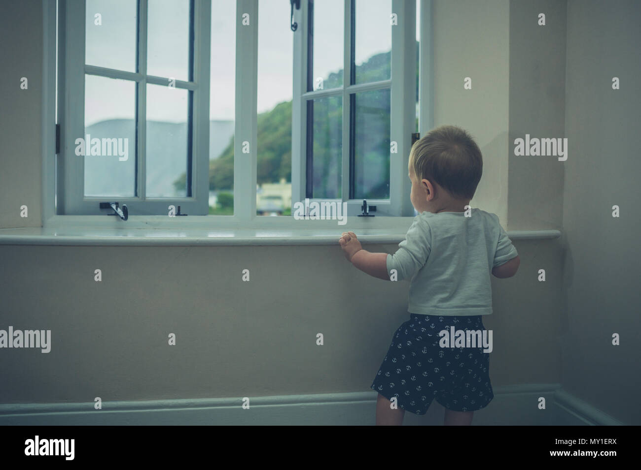 A cute little baby is standing by the window of a country house Stock ...