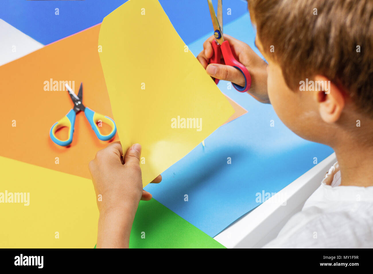 Child cutting colored paper with scissors at the table Stock Photo - Alamy