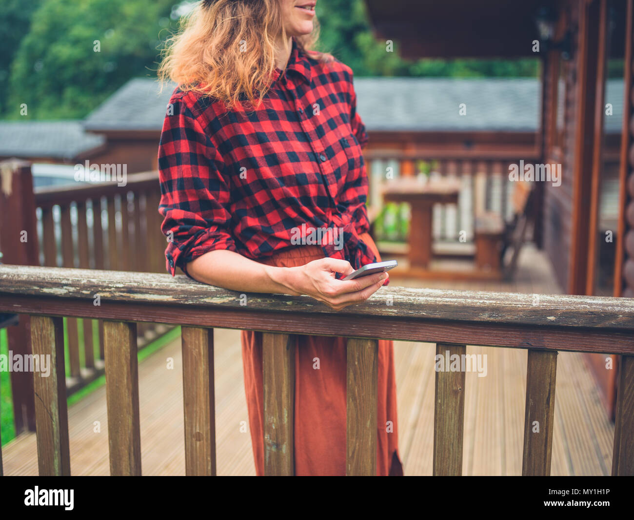 A young woman with a smart phone is standing on the porch of a log ...