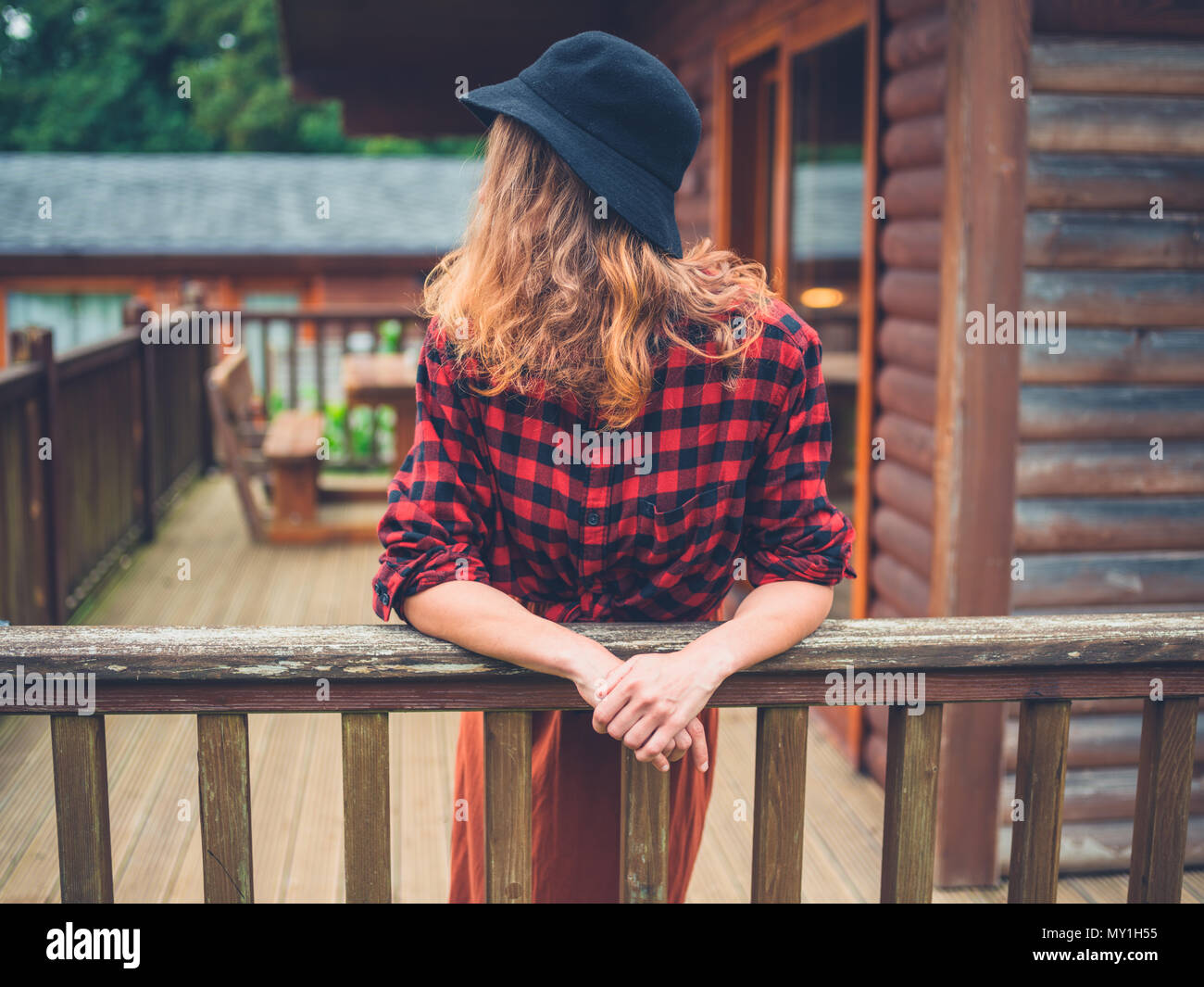A young woman wearing a hat is relaxing on the porch of a log cabin ...