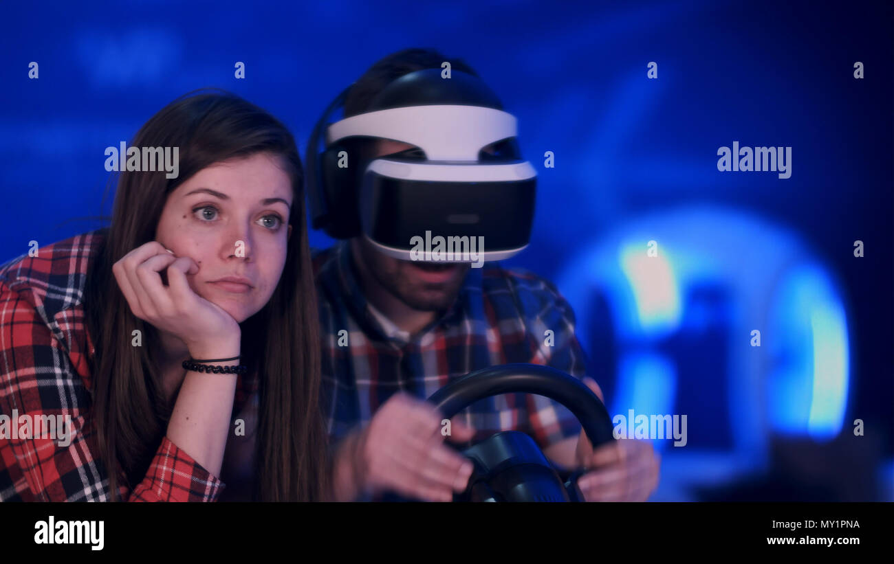 Slightly bored girl watching her excited boyfriend playing racing game ...