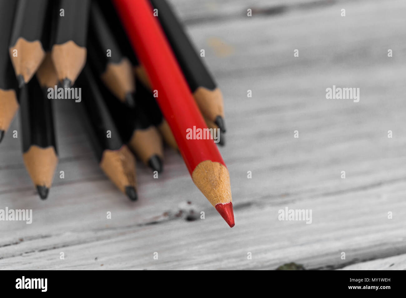 Red pencil stands out from the crowd of black pencil on a wooden white ...