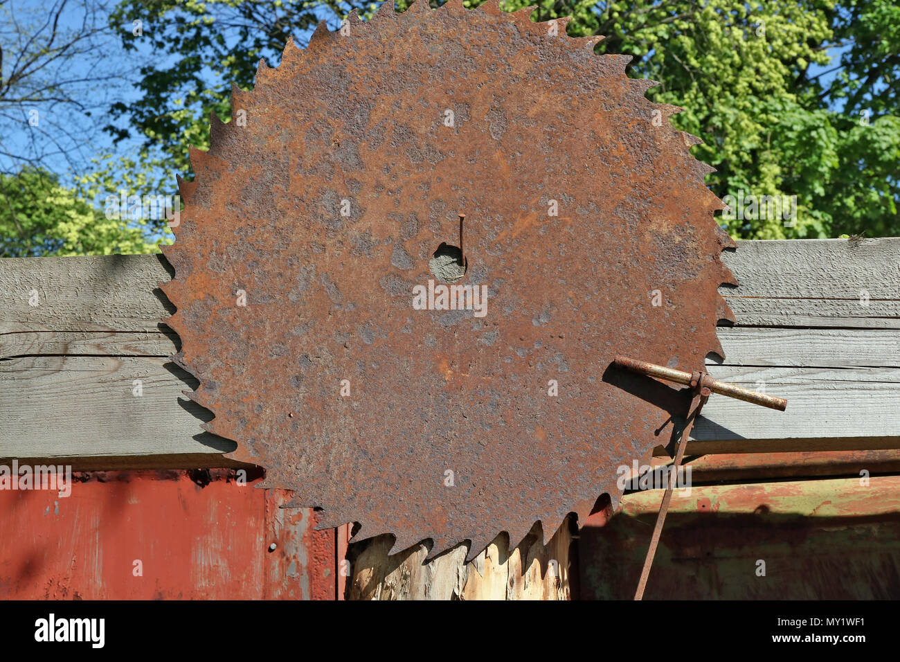 A huge rusty circular saw hanging on a rustic fence. Sunny spring day ...