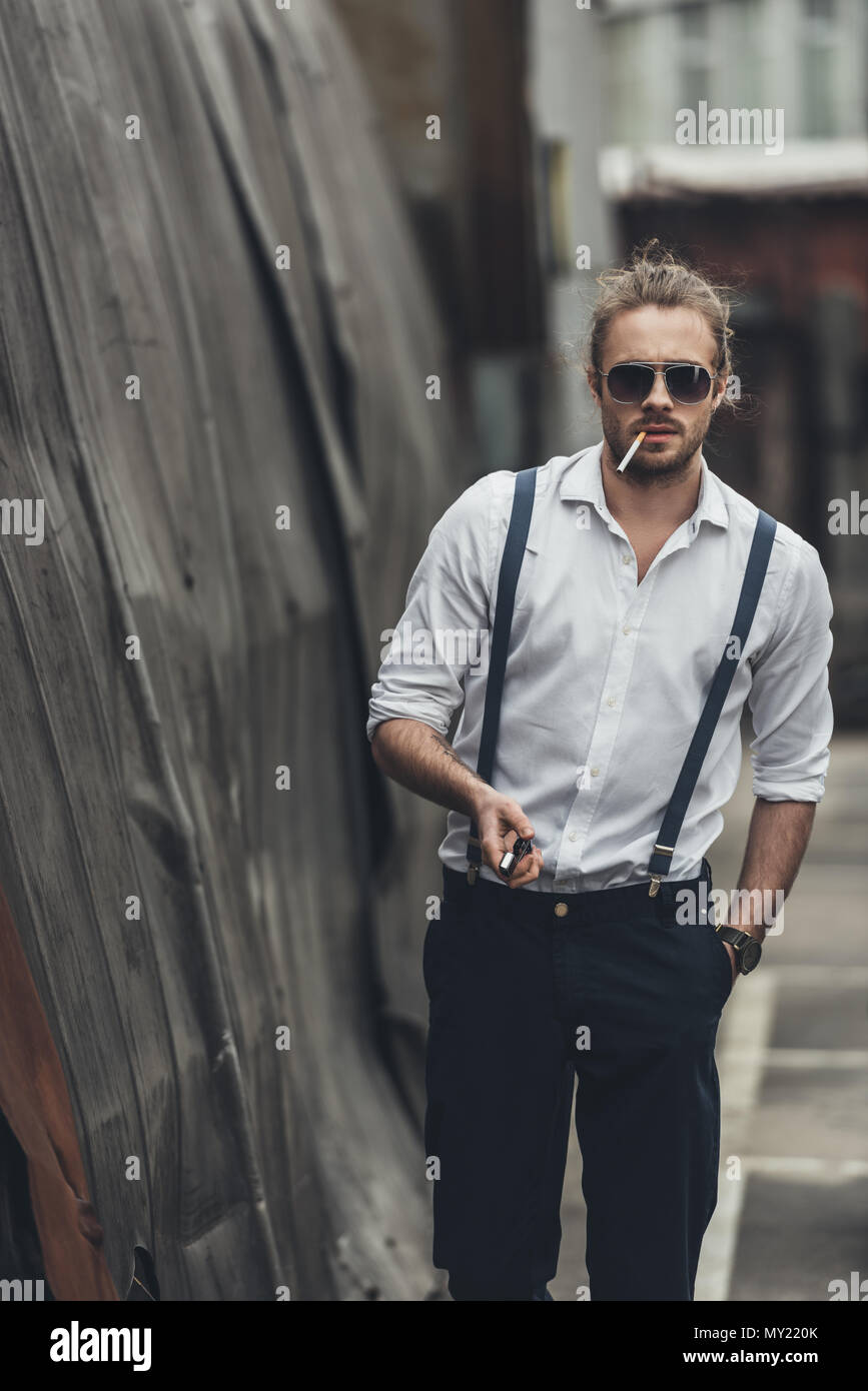 Stylish young man smoking cigarette and holding lighter while walking ...