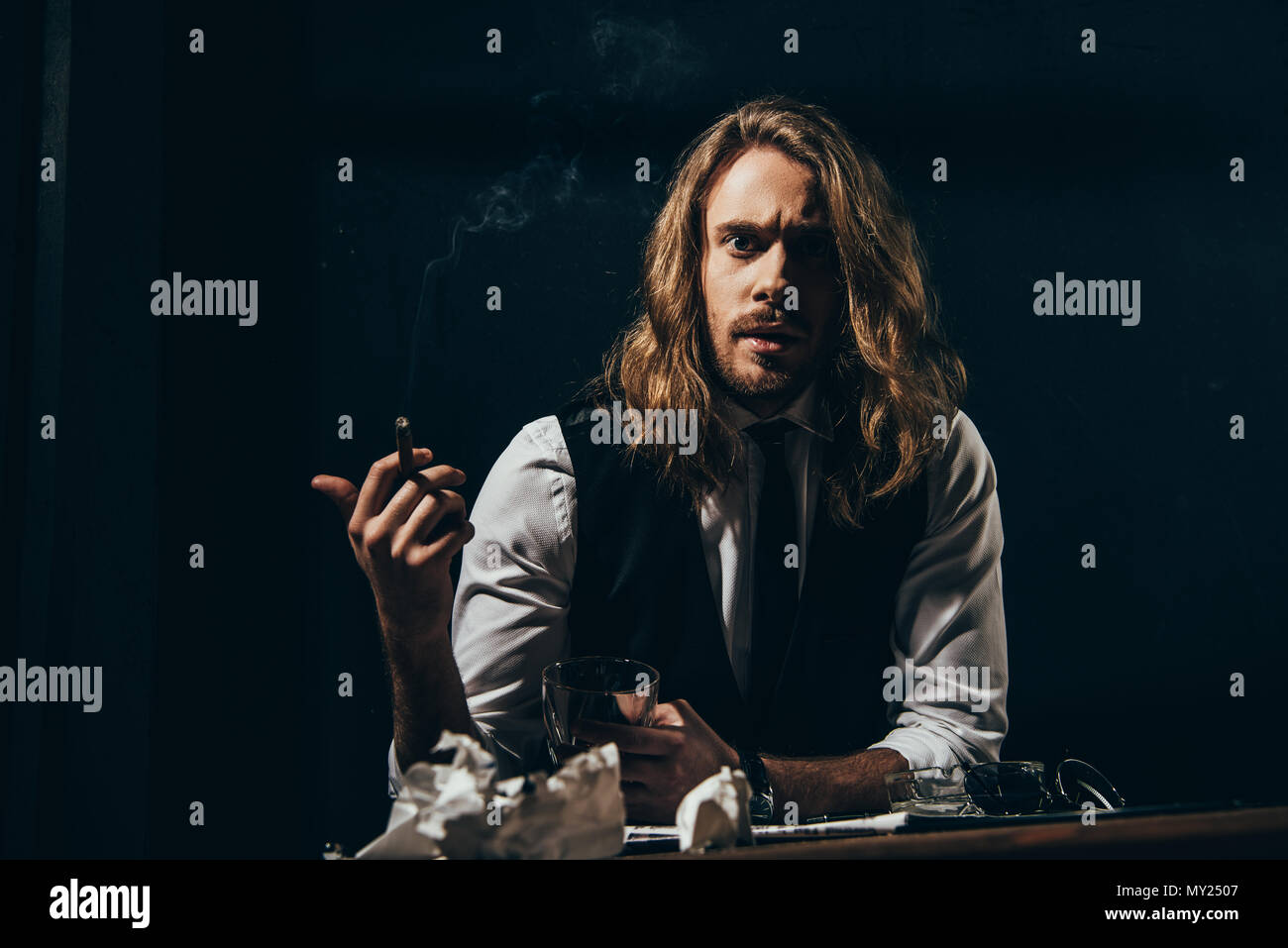 Bearded handsome long haired man in formal wear smoking cigar while ...