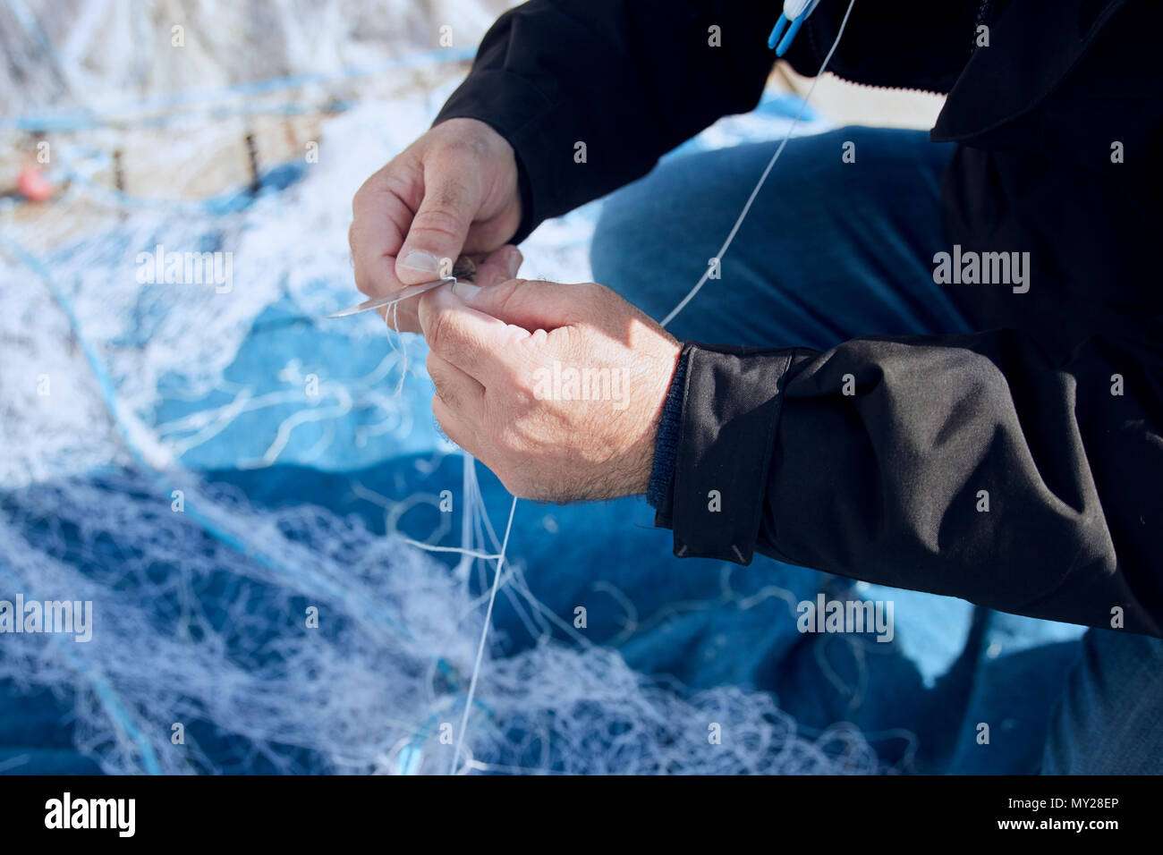 FHands of a fisherman repairing a fishing net with a net needle and ...