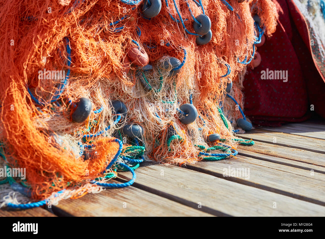 Pile of orange fishing net with blue rope and floats on the dock. Close ...
