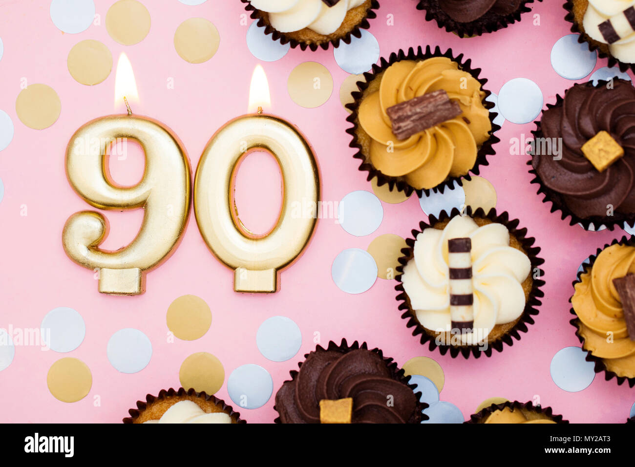Number 90 gold candle with cupcakes against a pastel pink background ...