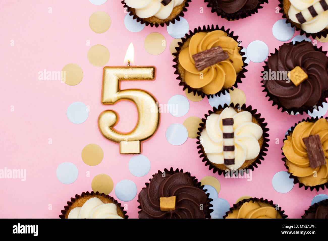 Number 5 gold candle with cupcakes against a pastel pink background ...