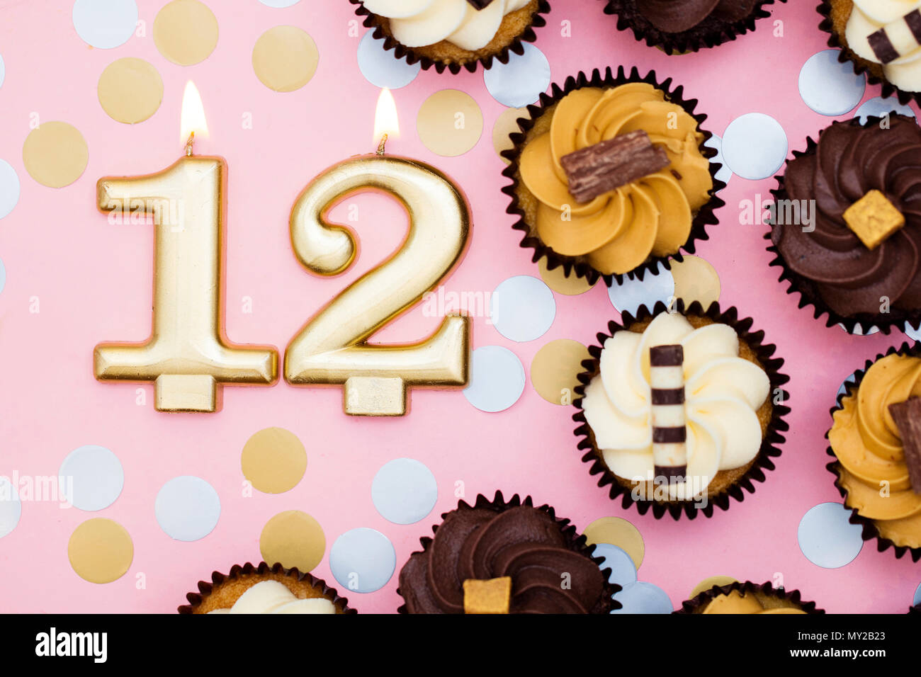 Number 12 gold candle with cupcakes against a pastel pink background ...