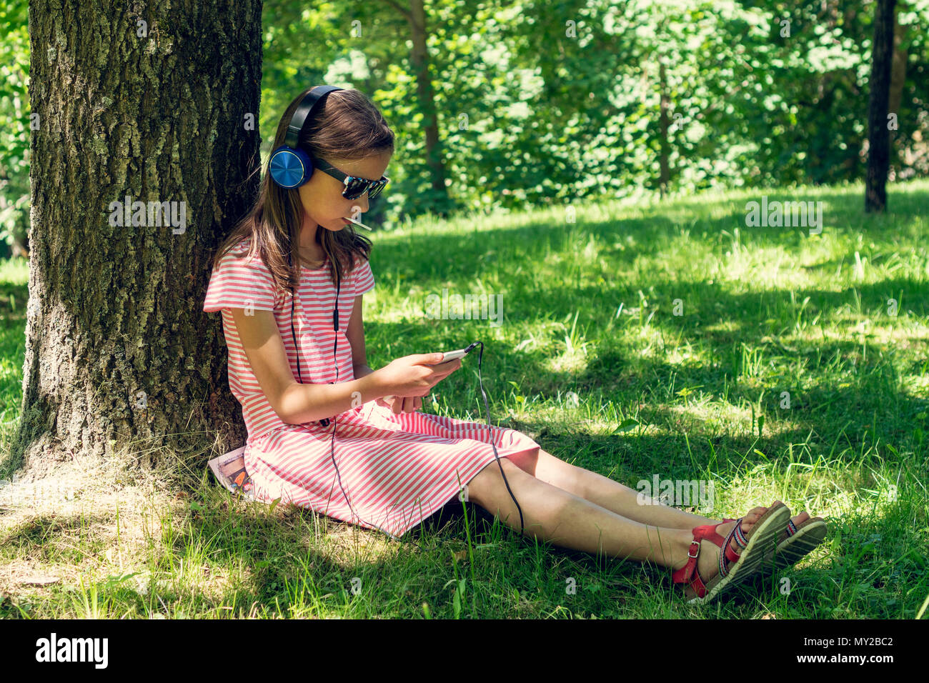 Girl listening to music under the tree shadow Stock Photo - Alamy