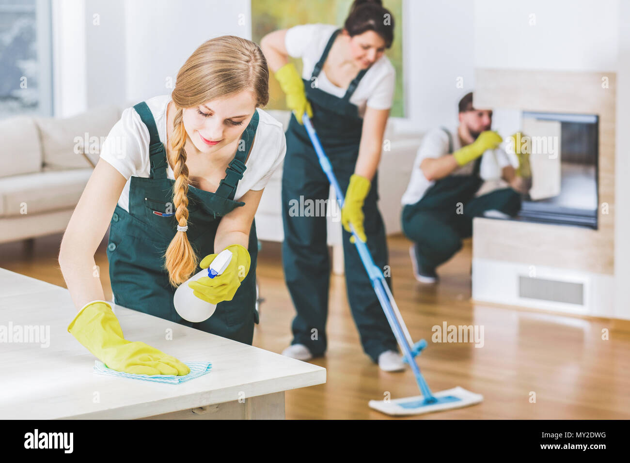 Young member of a cleaning crew wearing green overalls and yellow ...