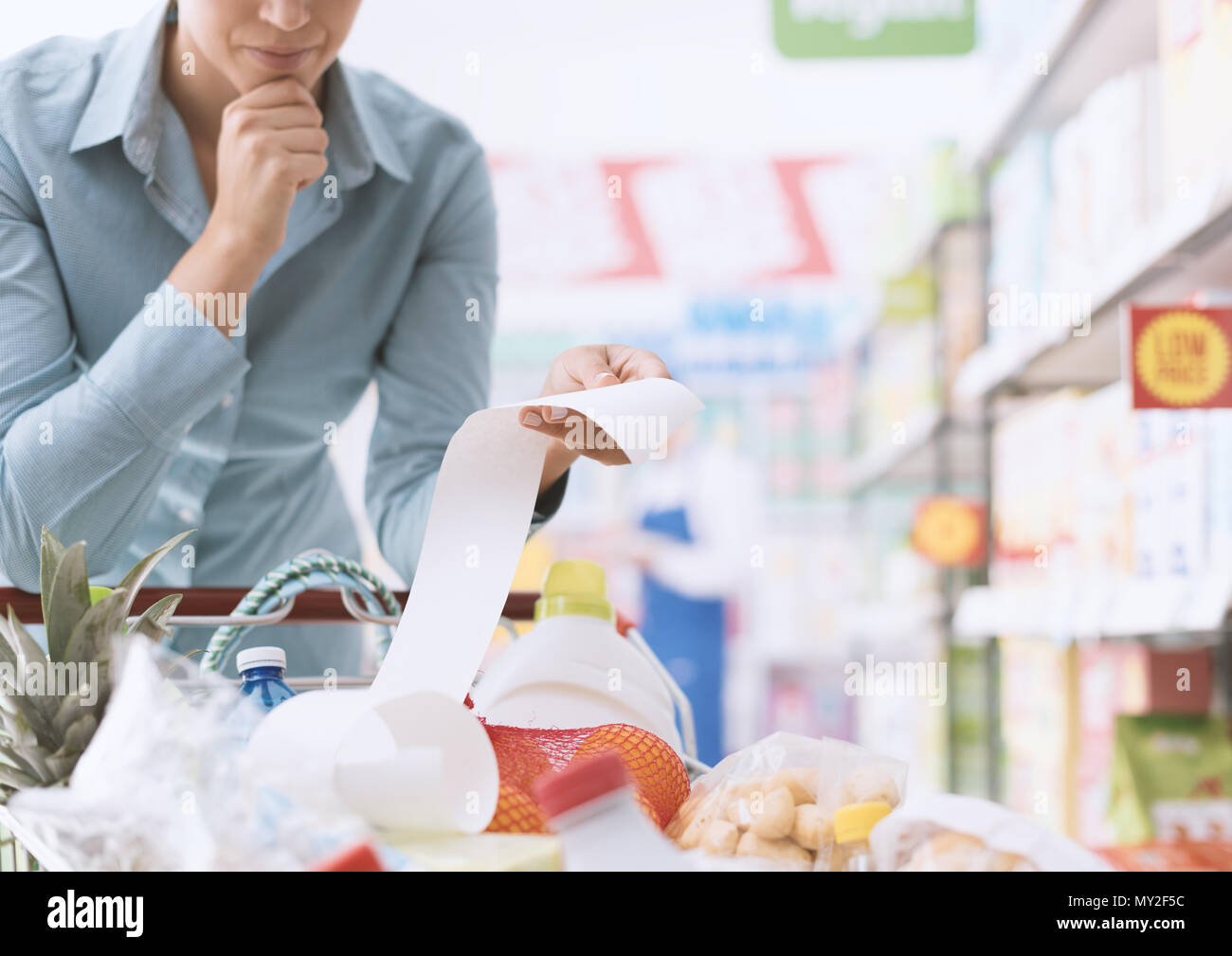 Woman checking the grocery receipt at the supermarket, she is concerned ...