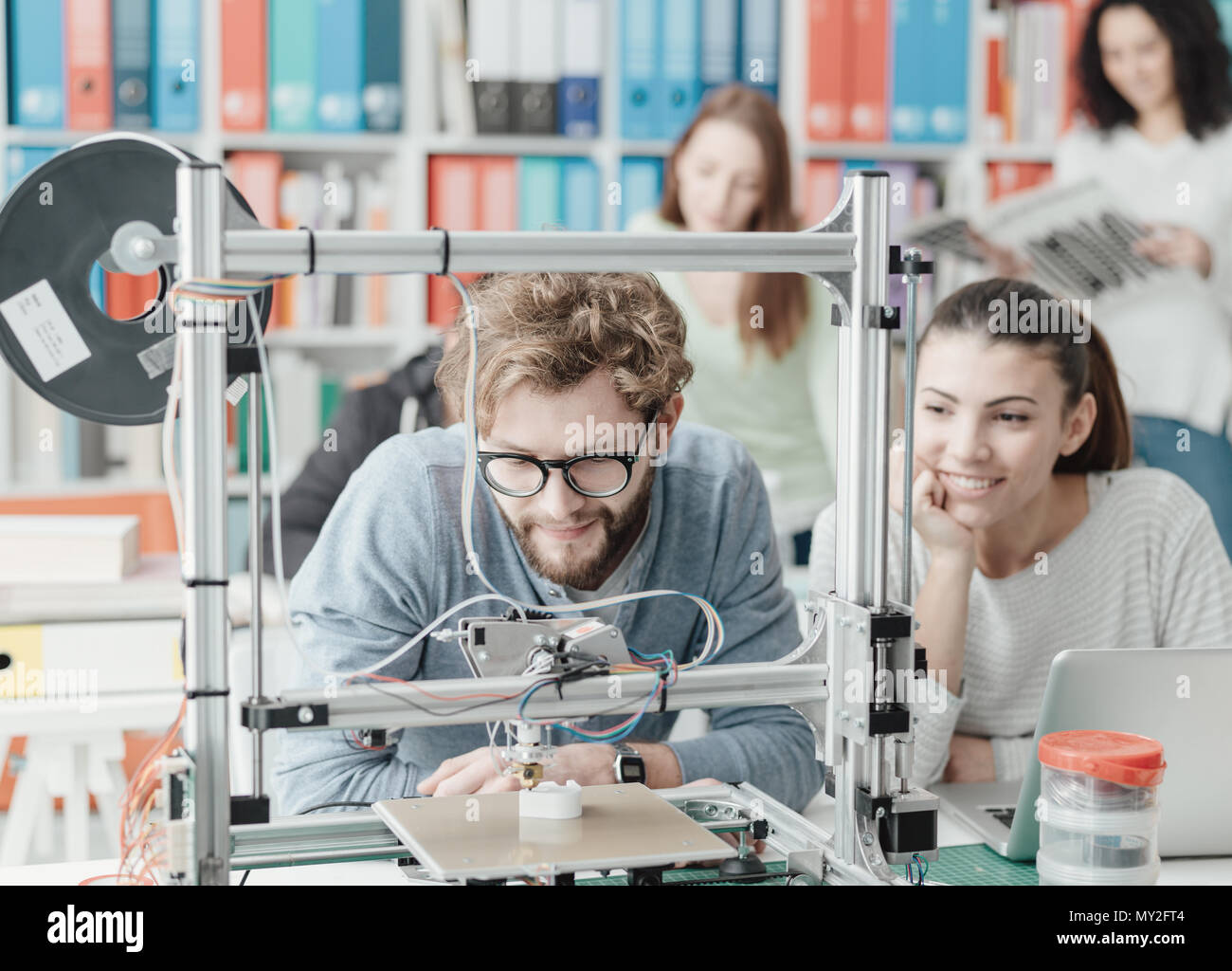 Male and female engineering students using a 3D printer in the lab ...
