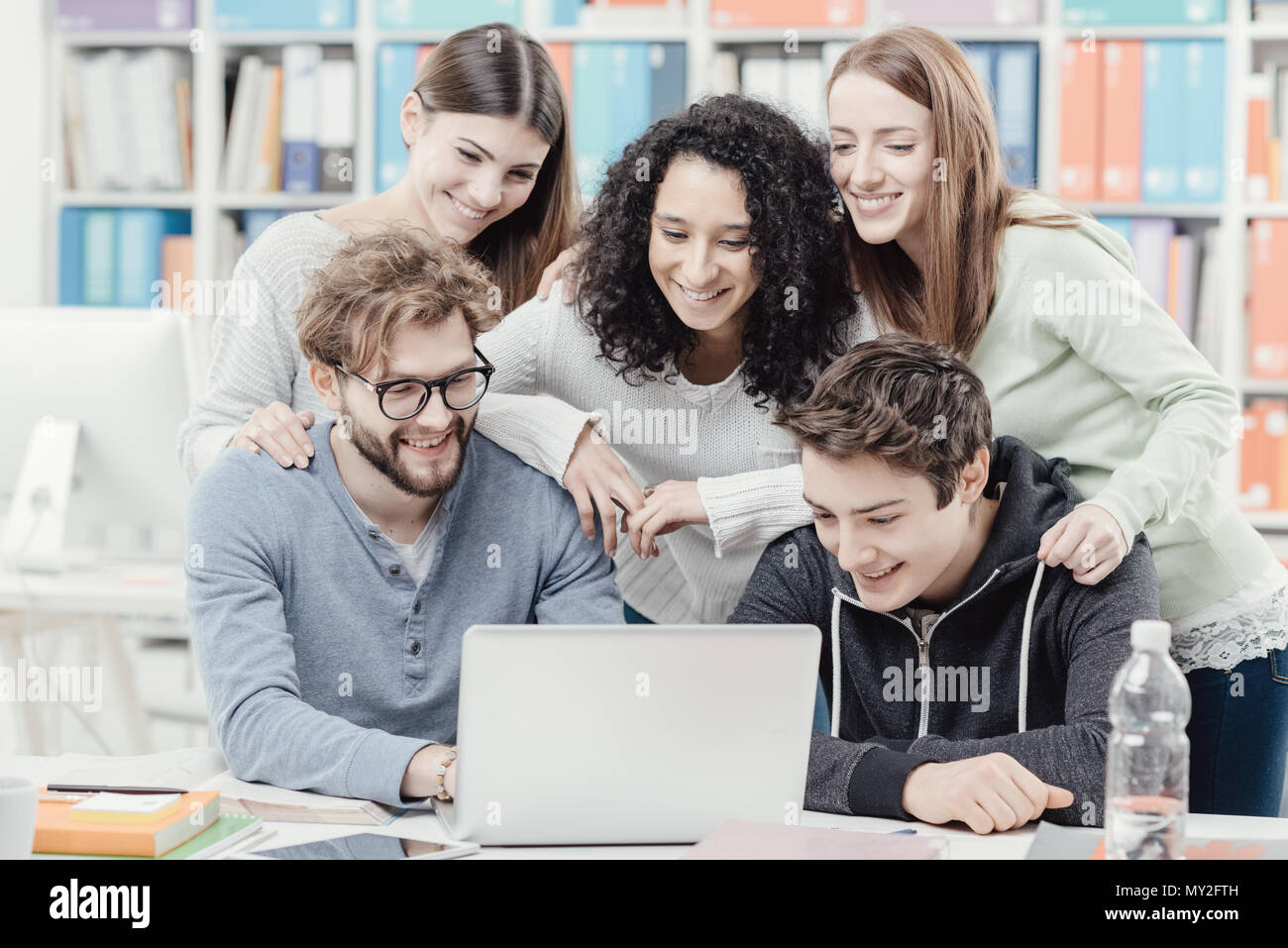 Group of happy students connecting together with a laptop and smiling ...