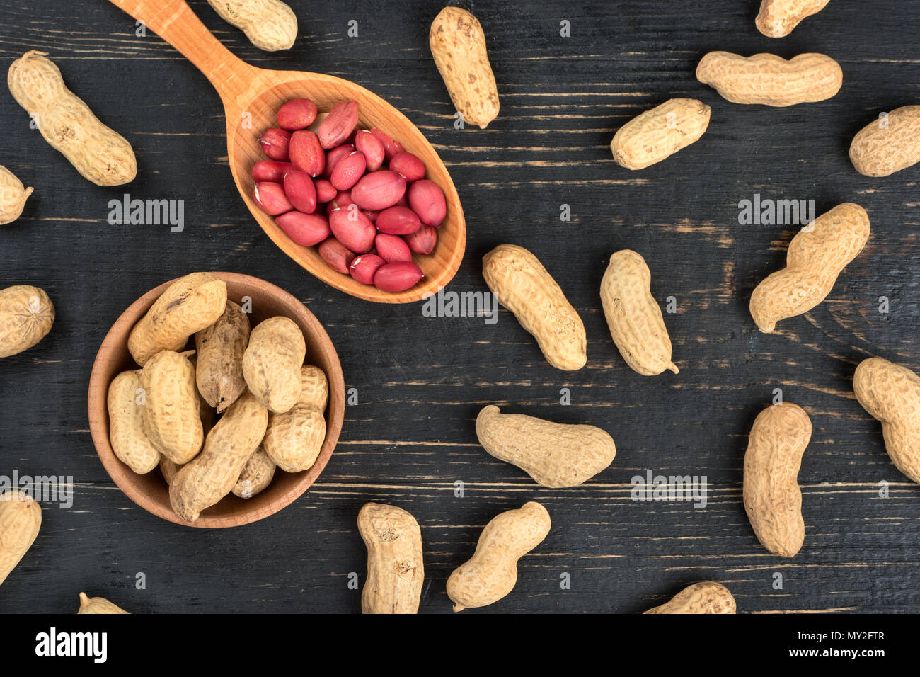 Peanuts in shell in a spoon, bowl and scattered on a wooden background ...